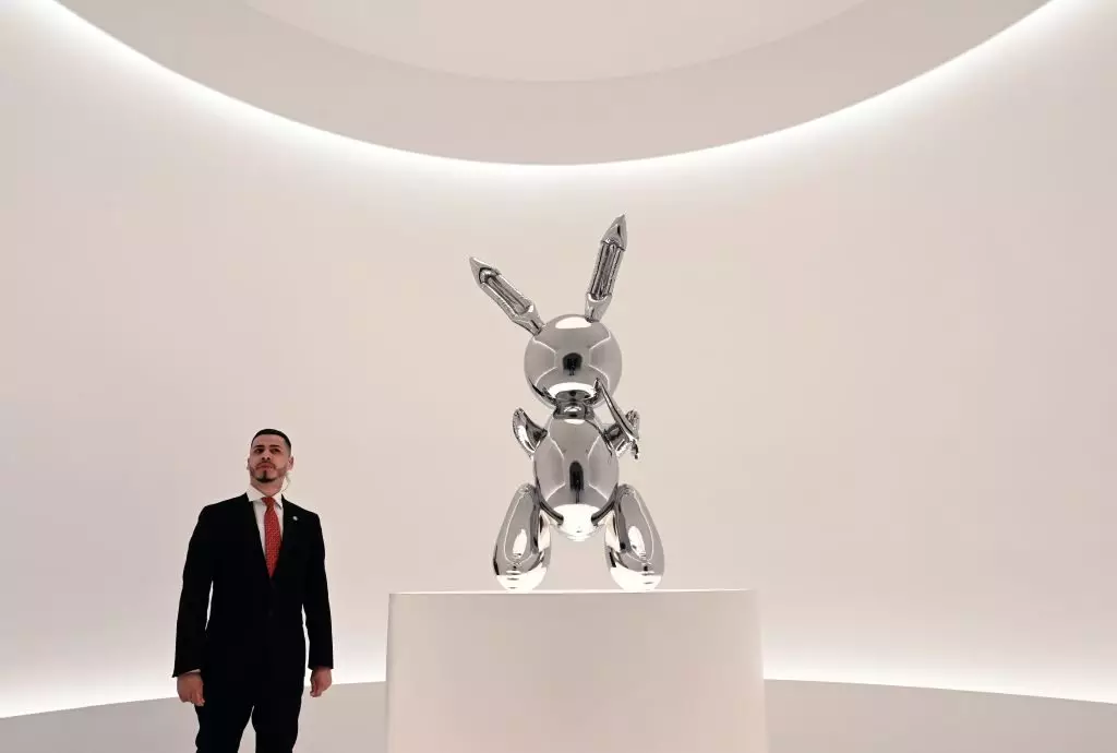 Umuzamu ahagaze iruhande rw'urukwavu rwa Jeff Koons kuva kuri