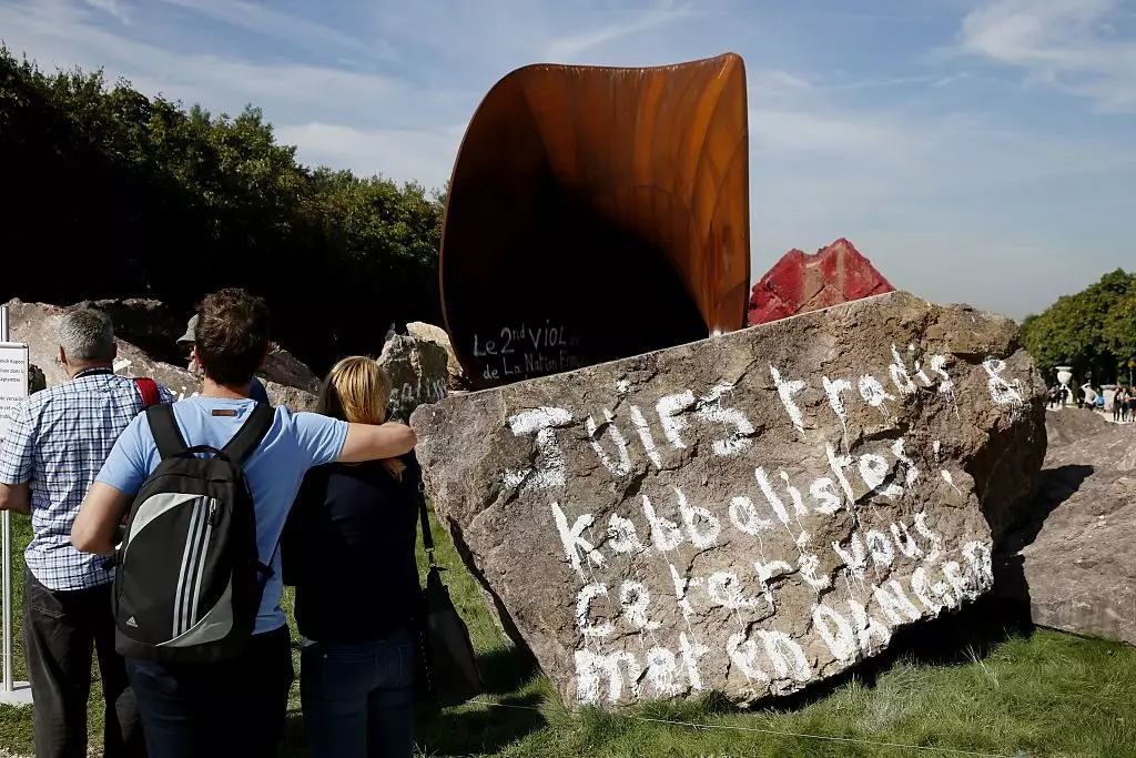 Die Menschen betrachten das mit Graffiti beschriftete Kunstwerk des britisch-indischen Künstlers Anish Kapoor mit dem Titel Dirty Corner in den Gärten des Chateau de Versailles in Versailles am 11. September 2015, einen Tag nachdem das Kunstwerk zum dritten Mal mit Graffiti verziert wurde. Mit freundlicher Genehmigung von Versailles Patrick Kovarik/AFP/Getty Images)