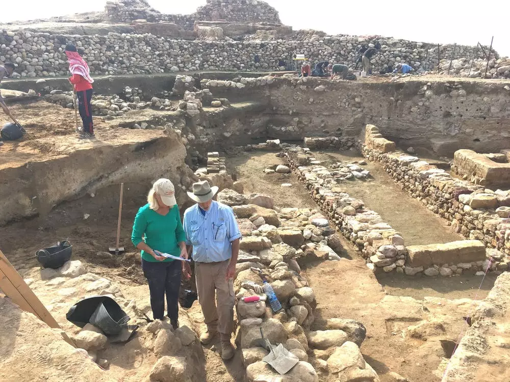 Studiuesit qëndrojnë pranë rrënojave të mureve të lashta të Tall el-Hammam, me shtresën e shkatërrimit afërsisht në mes të çdo muri të ekspozuar. Foto nga Phil Silvia, Creative Commons <a href=https://creativecommons.org/licenses/by-nd/4.0/ target=