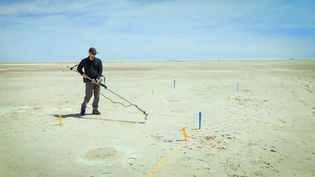 Mae Thomas Urban yn cynnal arolwg magnetomedr o olion traed mamoth yn White Sands. Llun gan David Bustos, trwy garedigrwydd Parc Cenedlaethol White Sands, New Mexico.