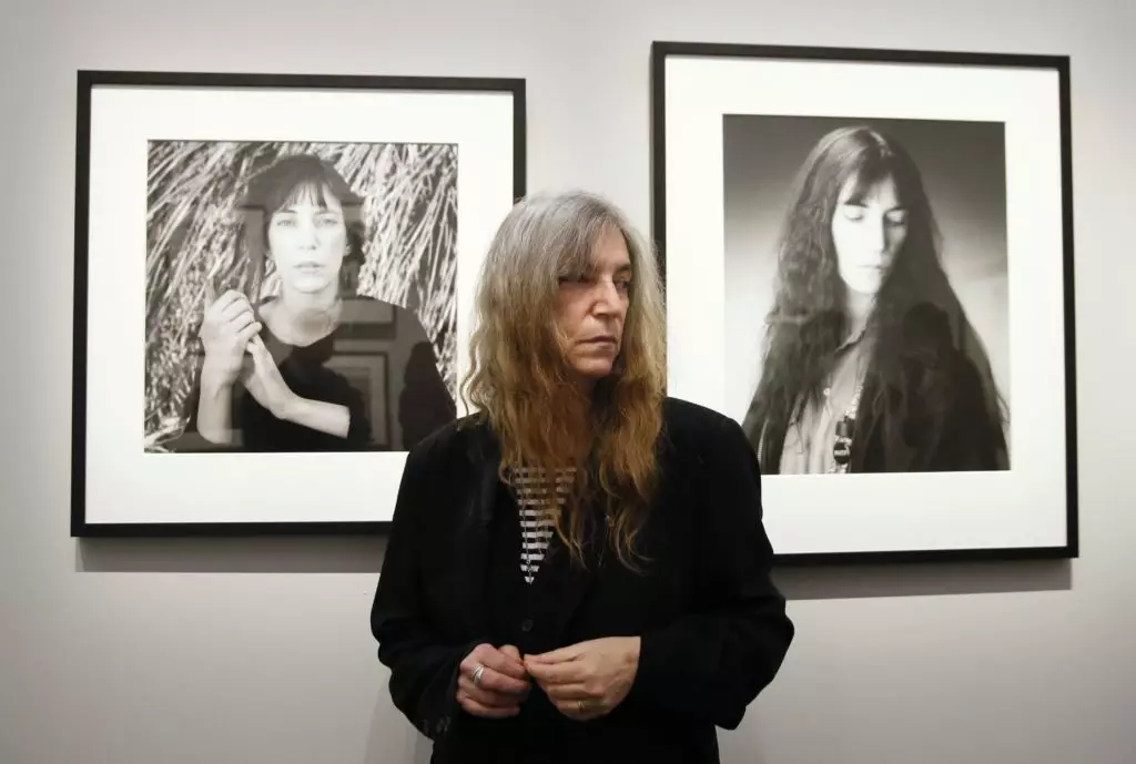 A musicista e autora Patti Smith posa na frente de seus retratos em uma exposição dedicada ao falecido Robert Mapplethorpe no Grand Palais em Paris. Cortesia de PATRICK KOVARIK/AFP/Getty Images.