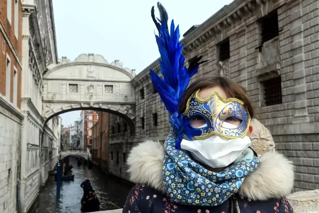 'n Jong toeris wat 'n beskermende gesigsmasker en 'n karnavalmasker dra, besoek Venesië. Foto deur Andrea Pattaro/AFP via Getty Images.