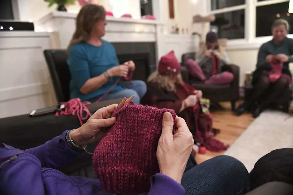 Ann Mitchell, solo se muestran las manos, da los toques finales a un gorro mientras, de izquierda a derecha en la parte de atrás, Jen Grant, Julie Piller y Debbie Asmus ayudan a tejer docenas de gorros rosas en la casa de Jen Grant el 15 de enero de 2019. 2017 en Lafayette, Colorado. Foto de Helen H. Richardson/The Denver Post vía Getty Images.