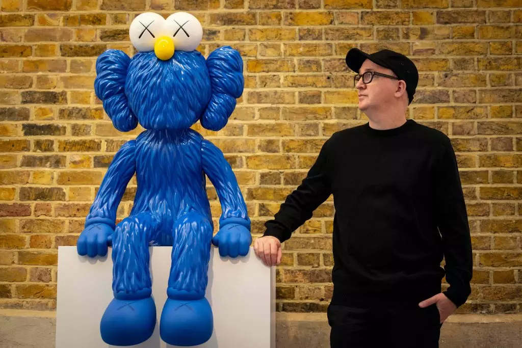 American artist KAWS, lub npe tiag tiag Brian Donnelly, poses nrog ib tug artwork hu ua SEEING thaum lub sij hawm ib tug xovxwm saib ua ntej rau lub exhibition 'KAWS: NEW FICTION' ntawm lub Serpentine North gallery nyob rau London thaum Lub ib hlis ntuj 18, 2022. COV ARTIST UPON PUBLICATION - TO ILLUSTRATE THE EVENT AS SPECIFIED IN THE CAPTION (Photo los ntawm Tolga Akmen / AFP) / txwv tsis pub siv EDITORIAL - MANDATORY MENTION OF THE ARTIST UPON PUBLICATION - KEV PAB CUAM TSHIAB - YUAV TSUM TAU TXAIS KEV THOV VAJTSWV TEJ LUS NYIAJ LUS - Qhia txog qhov xwm txheej raws li tau hais tseg hauv daim ntawv CAPTION (Duab los ntawm TOLGA AKMEN / AFP ntawm Getty Images)