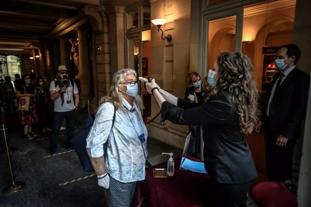 Seorang anggota staf memeriksa suhu tubuh pengunjung di pintu masuk pameran Turner di Museum Jacquemart-Andre di Paris pada 26 Mei 2020. Foto oleh Stephane De Sakutin/AFP via Getty Images.