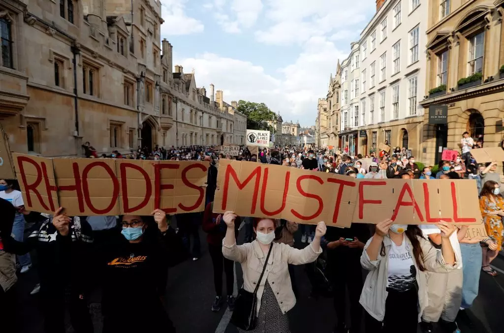 Demonstran memegang plakat selama protes yang diatur oleh kampanye 'Rhodes Must Fall', menyerukan penghapusan patung pengusaha Inggris dan imperialis Cecil John Rhodes, dari luar Oriel College di Universitas Oxford. Foto oleh Adrian Dennis/AFP melalui Getty Images.