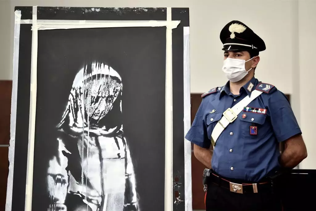 Tá Carabiniere Iodálach in aice le píosa ealaíne a cuireadh i leith Banksy, a goideadh ag an Bataclan i bPáras in 2019, agus a fuarthas i dteach feirme tréigthe in Abruzzo. Grianghraf le FILIPPO MONTEFORTE/AFP trí Getty Images.