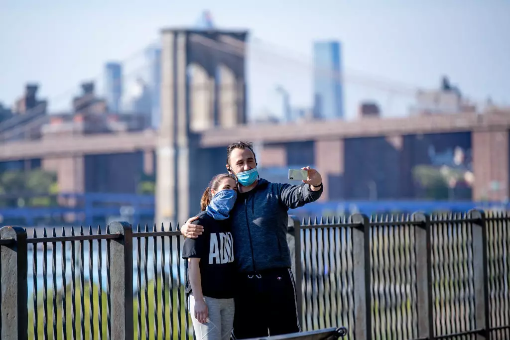 Os visitantes fanse unha selfie e usan máscaras no Brooklyn Heights Promenade coa ponte de Brooklyn ao fondo o 10 de maio de 2020 na cidade de Nova York. Foto de Roy Rochlin/Getty Images.