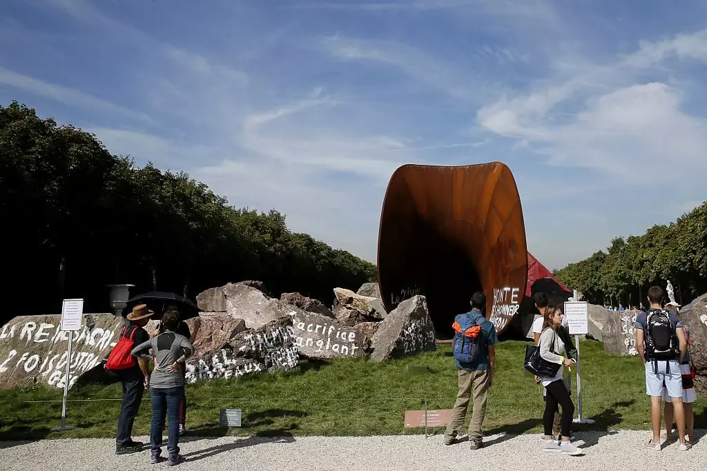 Oamenii se uită la opera de artă inscripționată cu grafitti a artistului britanic-indian Anish Kapoor intitulată