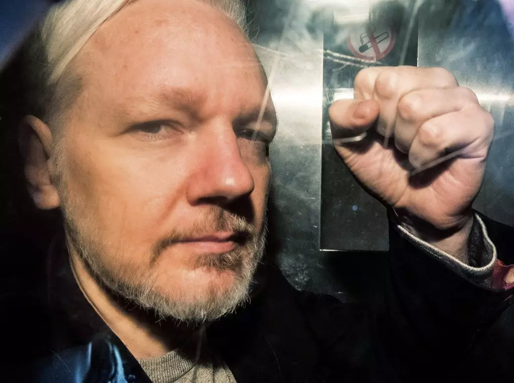 Julianas Assange'as gestikuliuoja pro kalėjimo furgono langą, kai 2019 m. gegužės 1 d. įvaromas į Southwark Crown Court Londone, o vėliau buvo nuteistas 50 savaičių kalėti už tai, kad 2012 m. pažeidė užstato sąlygas. (Danielio LEAL / AFP nuotrauka) (Nuotrauka DANIEL LEAL / AFP per Getty Images)