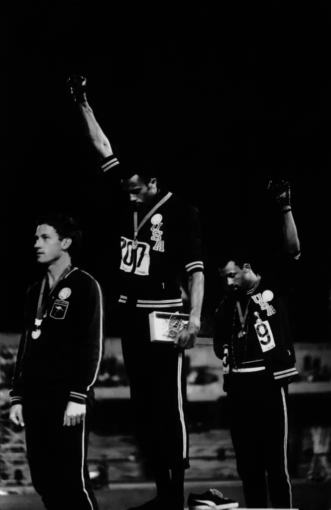 Nuotrauka, kurioje 1968 m. olimpinėse žaidynėse ant prizininkų pakylos atsistoja Tommie Smithas ir Johnas Carlosas, žiūrintys žemyn ir iškėlę kumštį. Nuotrauka © Time & Life Pictures / Getty Images.