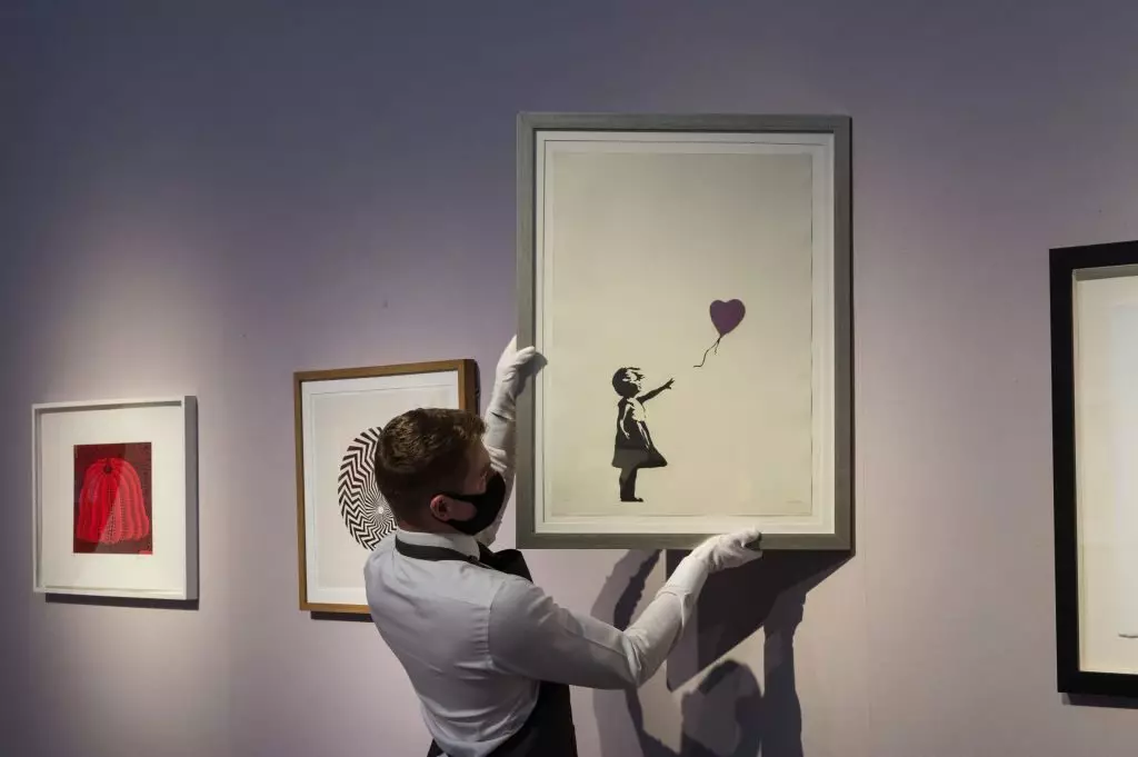 Starfsmaður heldur uppi Banksy's Girl with Balloon á Christie's. Mynd eftir Wiktor Szymanowicz/Barcroft Media í gegnum Getty Images.