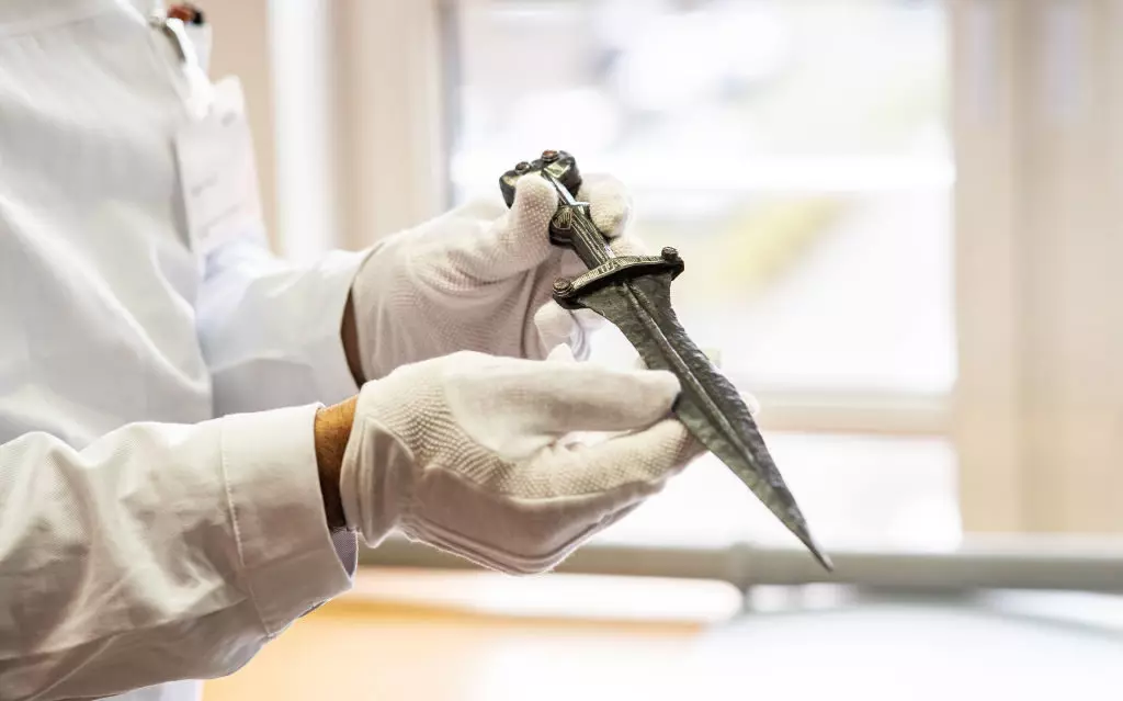 Umbuyiseli we-LWL-Archaeology yase-Westphalia uphethe i-2000 ye-dagger yomkhosi ezandleni zakhe eMntla Rhine-Westphalia, eMünster ngoFebruwari 14, 2020. Ifoto: Guido Kirchner/dpa nge-Getty Images.