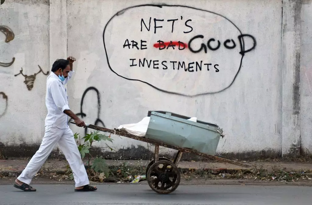 Mae deliwr sgrap yn India yn gwthio ei handcart heibio graffiti NFT. (Llun gan Ashish Vaishnav/SOPA Images/LightRocket trwy Getty Images)