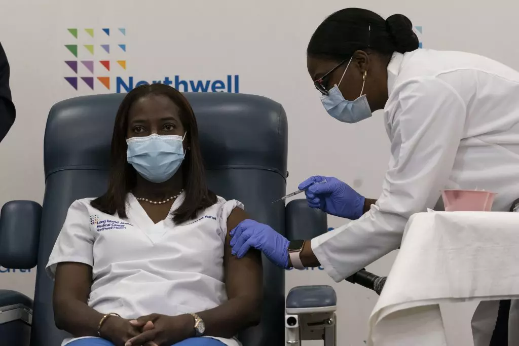 Sandra Lindsay, kénca, perawat di Pusat Médis Yahudi Long Island, disuntik ku vaksin COVID-19 ku Michelle Chester, 14 Désémber 2020 di wilayah Queens di New York City. Ngaluncurkeun vaksin Pfizer sareng BioNTech, anu munggaran disatujuan ku Administrasi Pangan sareng Narkoba, ngiringan usaha vaksinasi pangbadagna dina sajarah AS. (Poto ku Mark Lennihan Pool/Getty Images.