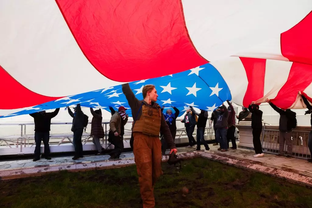 Yon gwoup manifestan pro-Trump leve yon drapo jeyan Amerik sou teren West nan Bilding Kapitòl la nan dat 6 janvye 2021 nan Washington, DC. Foto pa Jon Cherry / Geti Images.