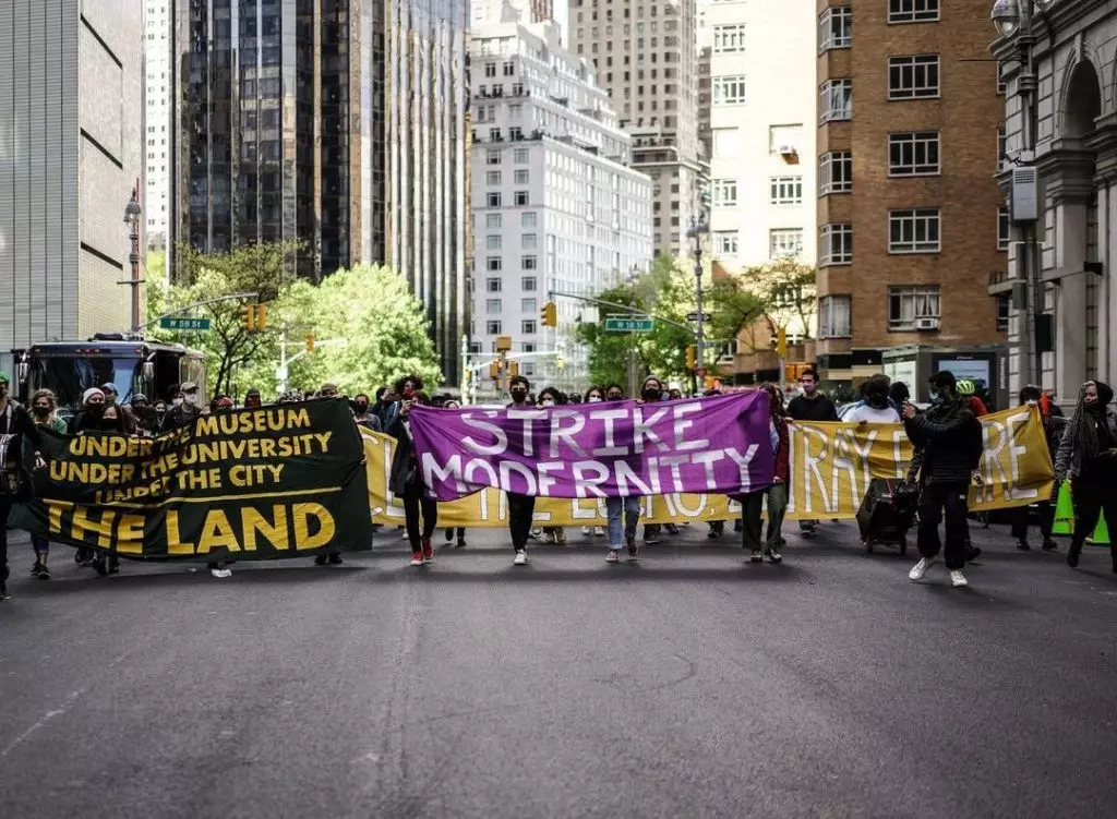 Batu manifestaciantojn de MoMA marŝantajn tra la urbocentro de Novjorko. Ĝentileco de Decolonize This Place per Twitter.